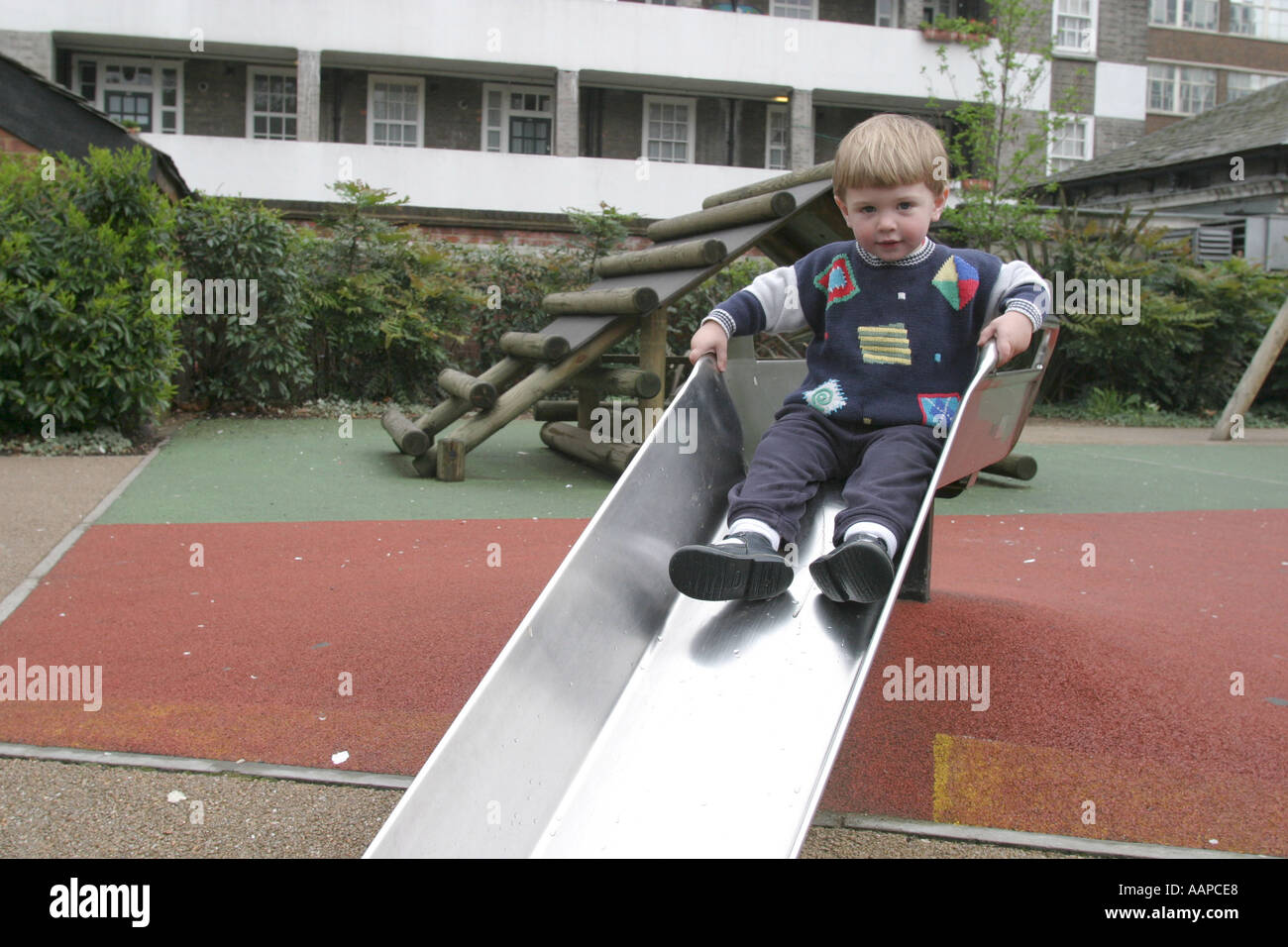 Smiling Young boy playing on slide in children's playground ...