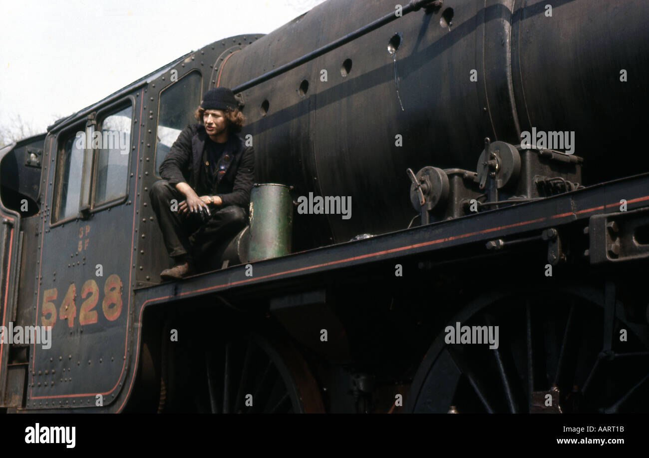 Man in overalls on side of large steam locomotive at a railway ...