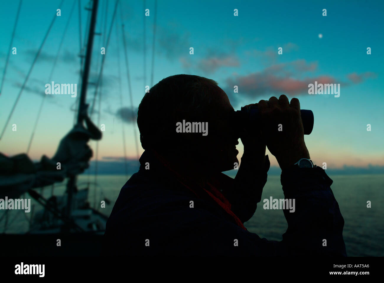 A sailor on an ocean passage searches the horizon with binoculars from ...