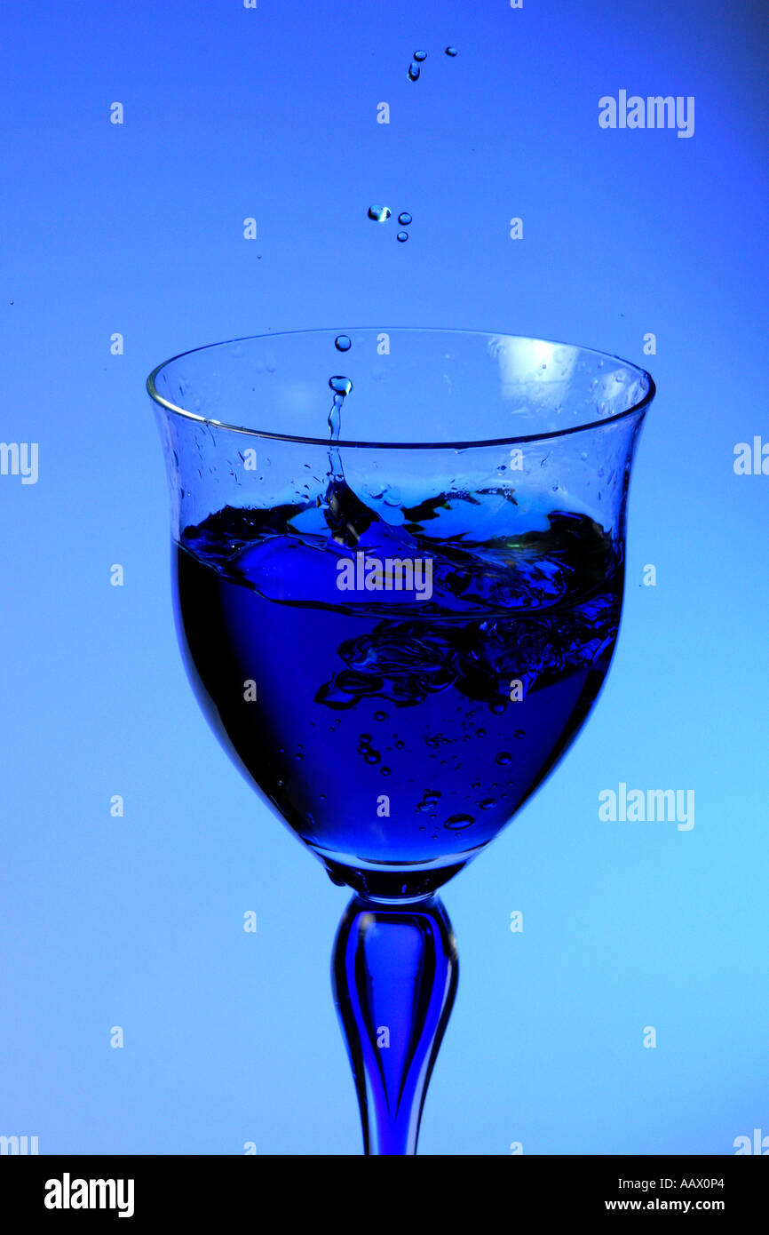 Action shot of water dripping into glass with blue filtered lighting ...