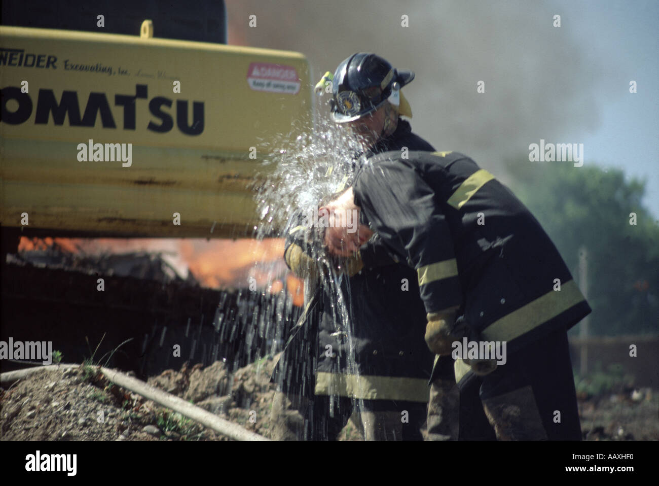 Fire Fighter with hose cooling off another fire fighter at a scene of a ...
