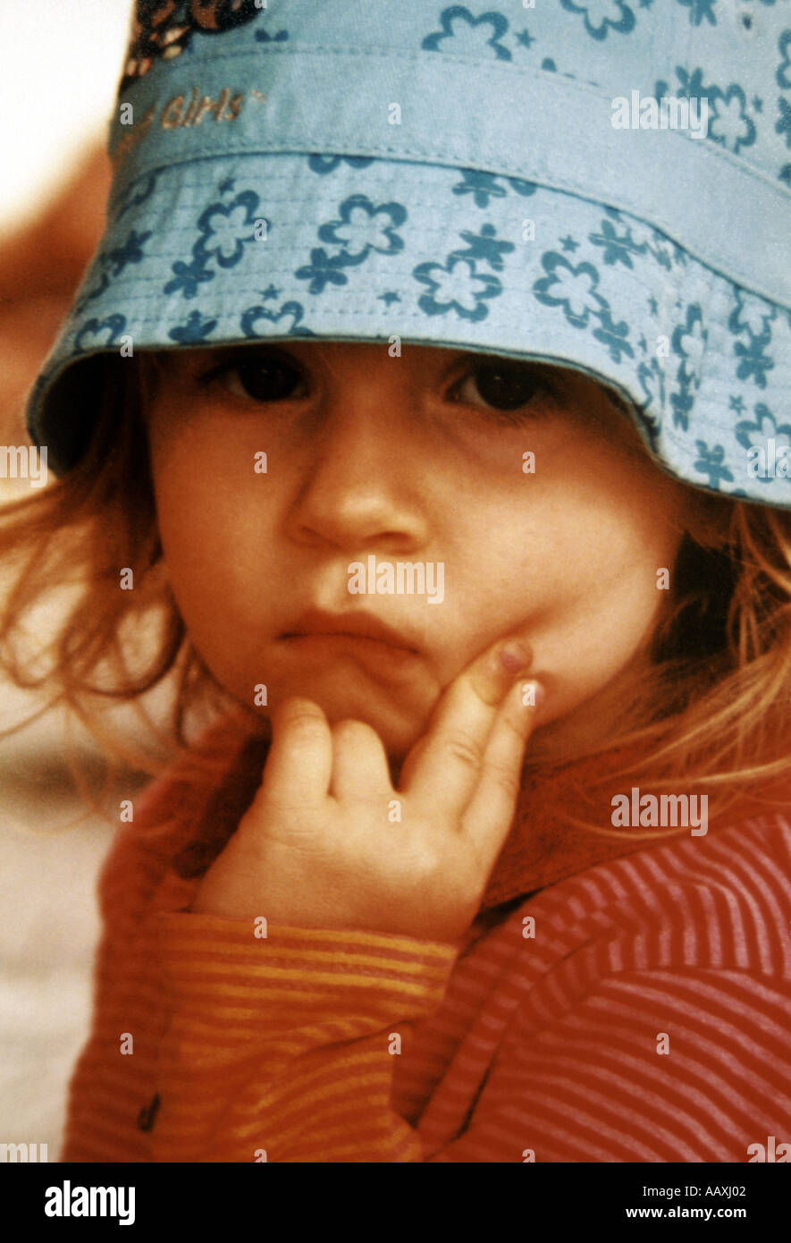 Little girl in blue hat with fingers on chin looking very sad Stock ...