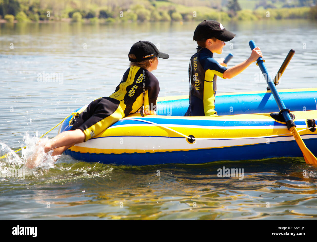 two boys 6 wearing wetsuits playing in an inflatable boat on lake Stock ...