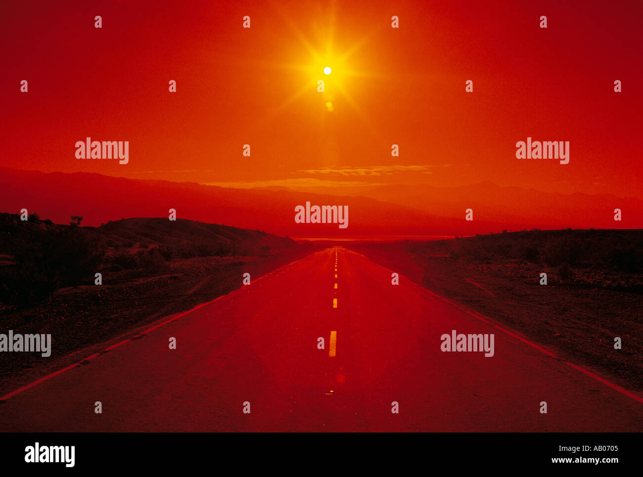 Orange filtered shot of the sun hanging directly over empty two lane ...