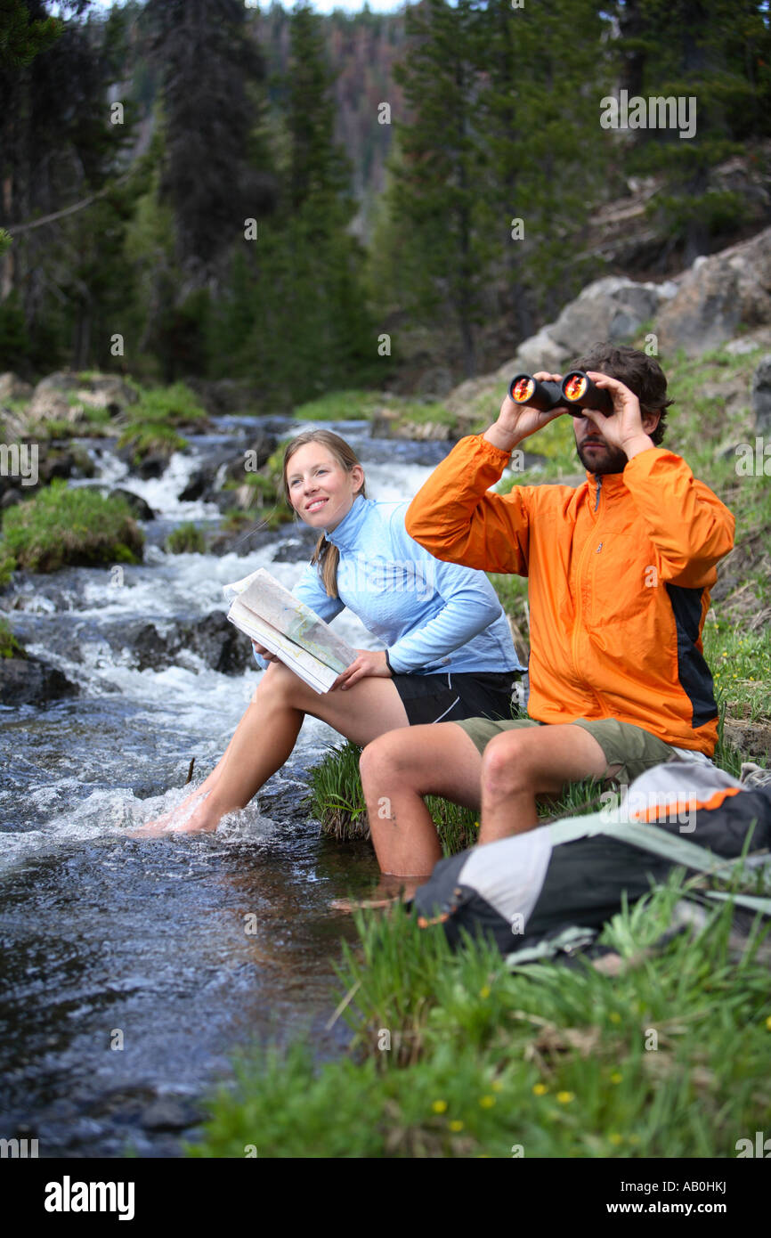 Backpacking couple sit down by a stream to look at map Stock Photo - Alamy