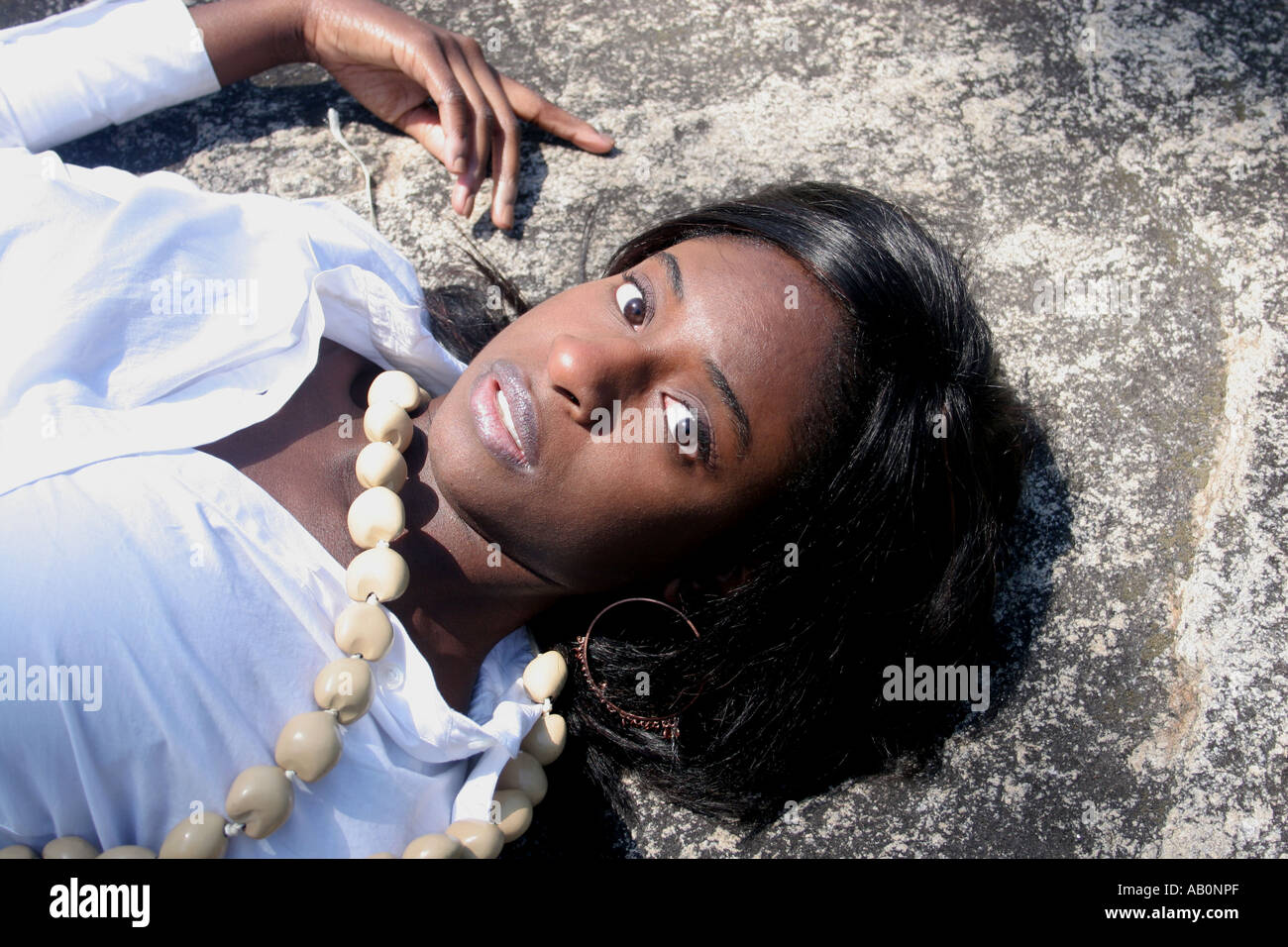 African American woman, early 20s supine on rock, eye contact with ...