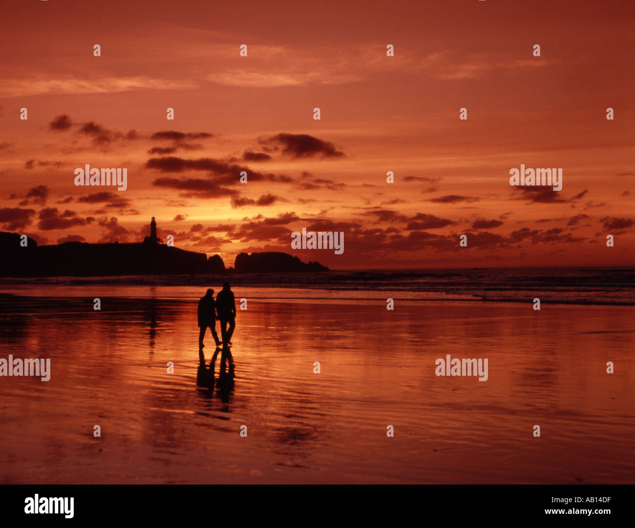 Sunset silhouette of two beach walkers on a shimmering stretch of wet ...
