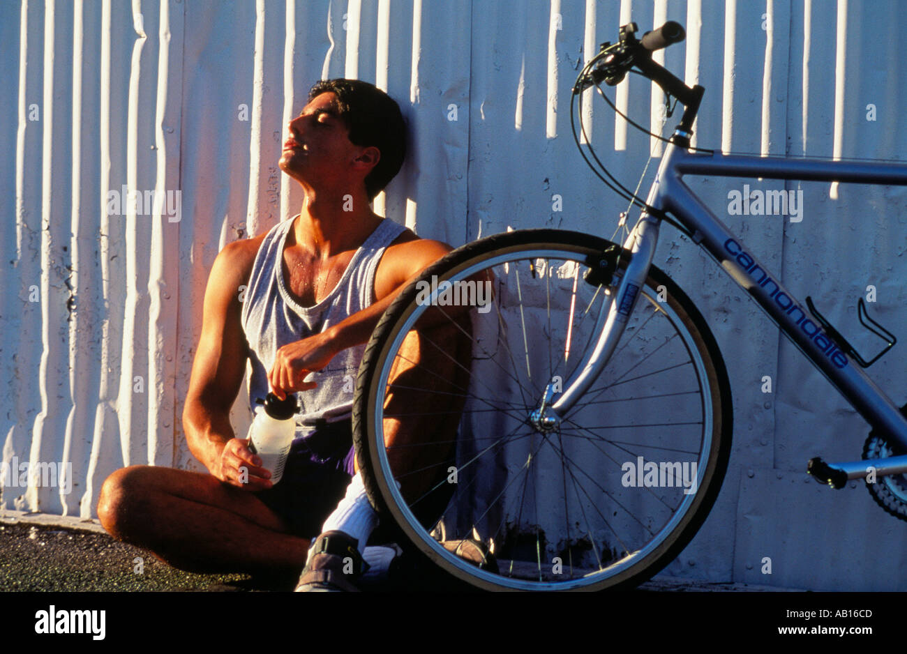Exhausted man dripping with sweat sitting beside his mountain bike ...