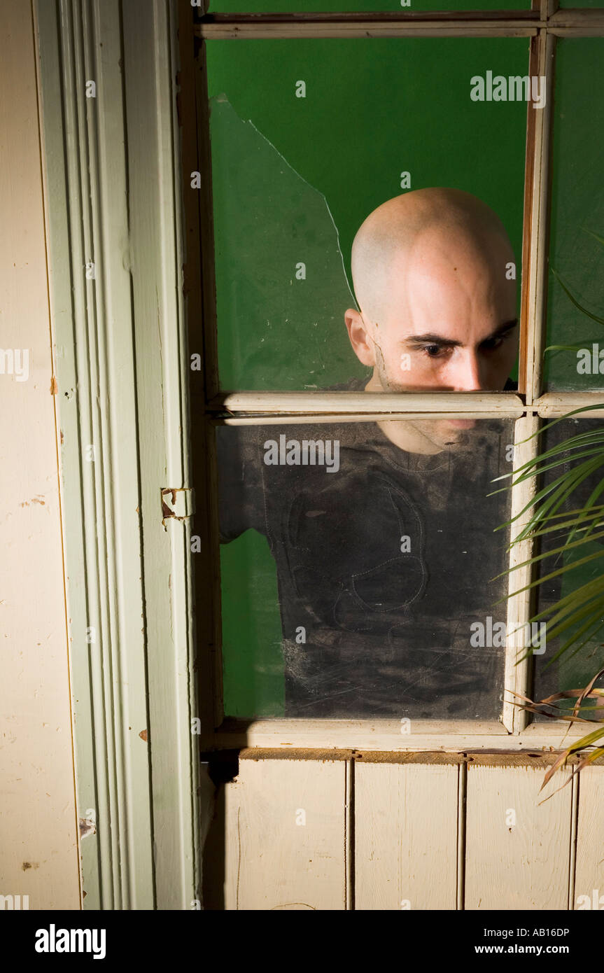 Sinister character peering through a broken window Stock Photo - Alamy