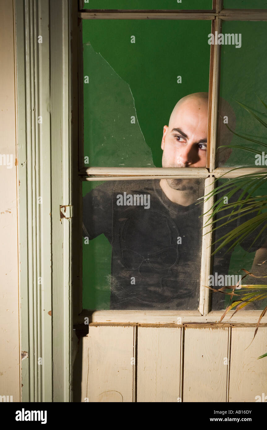 Sinister character peering through a broken window Stock Photo - Alamy