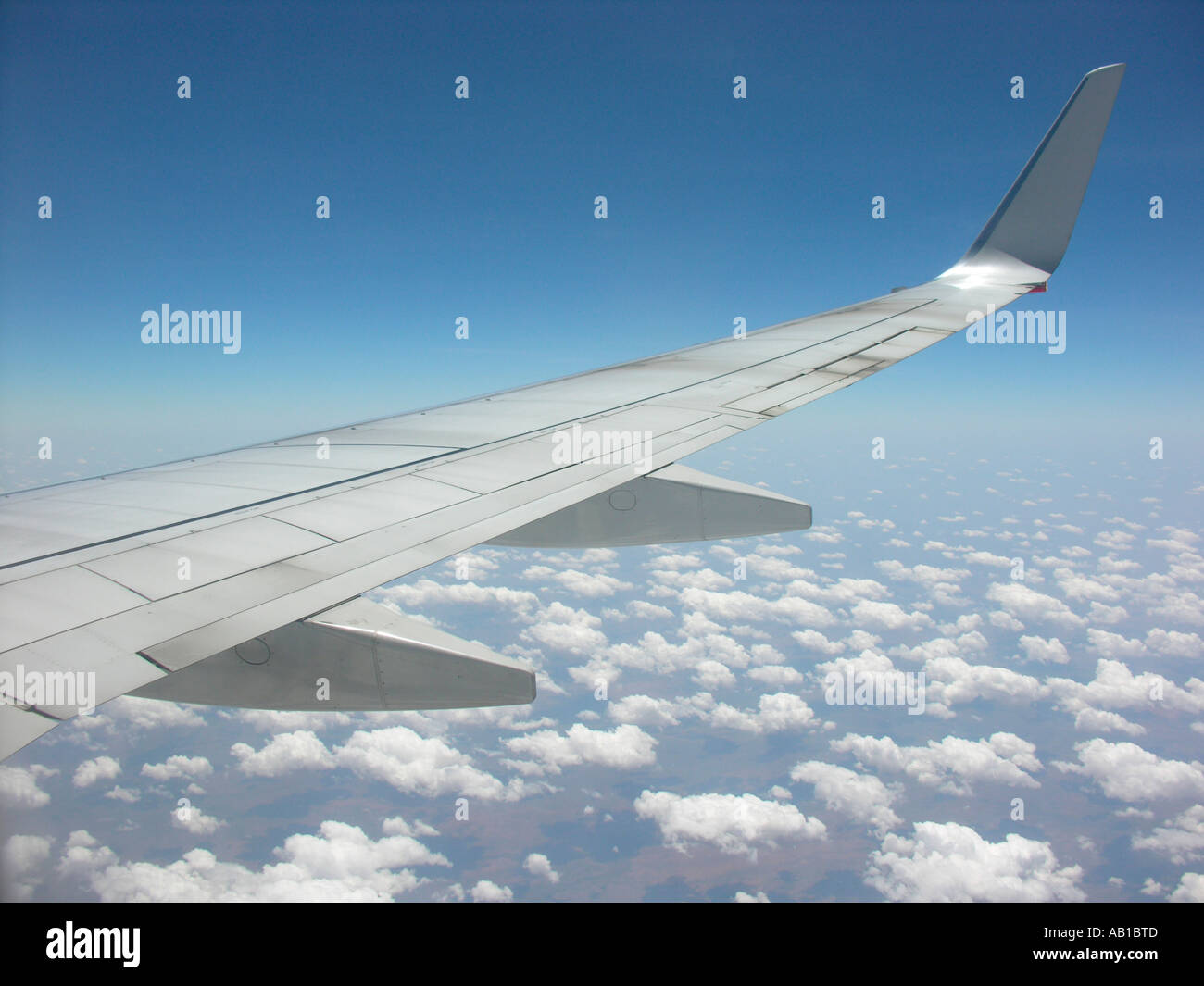 Bent wing of aeroplane with two turbines airborne above fluffy clouds ...