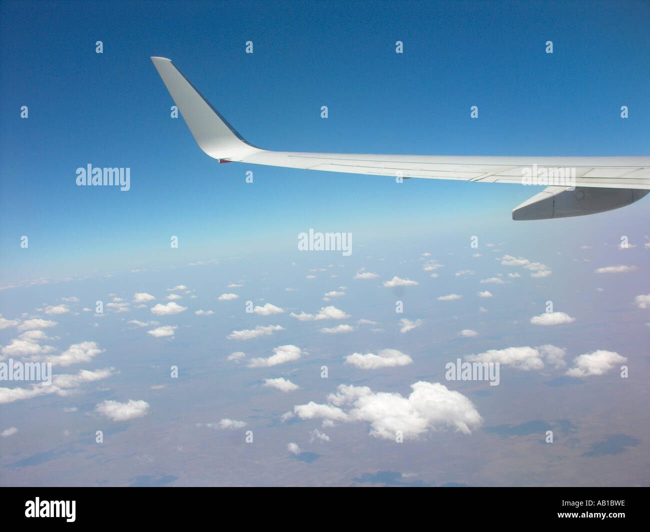 Bent wing of aeroplane with one turbine airborne above fluffy clouds ...
