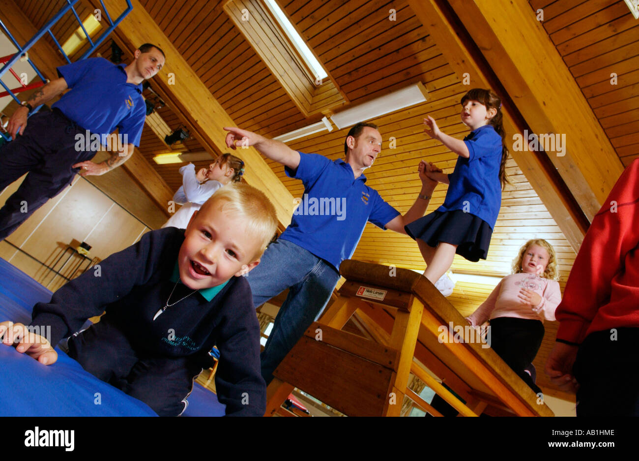 Fathers helping pupils with exercise running jumping in gym at after ...