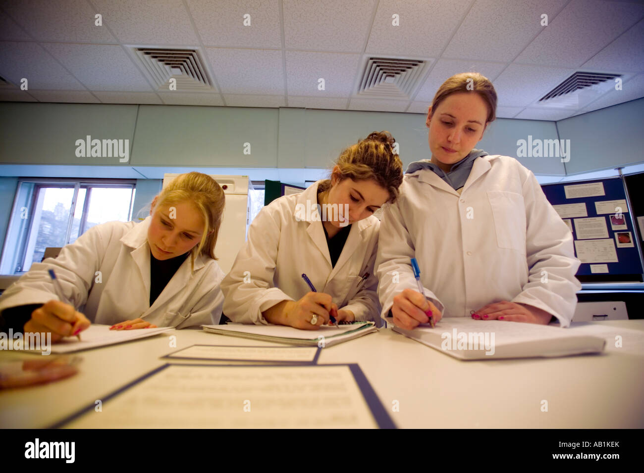 three science students in lab writing up notes Stock Photo - Alamy