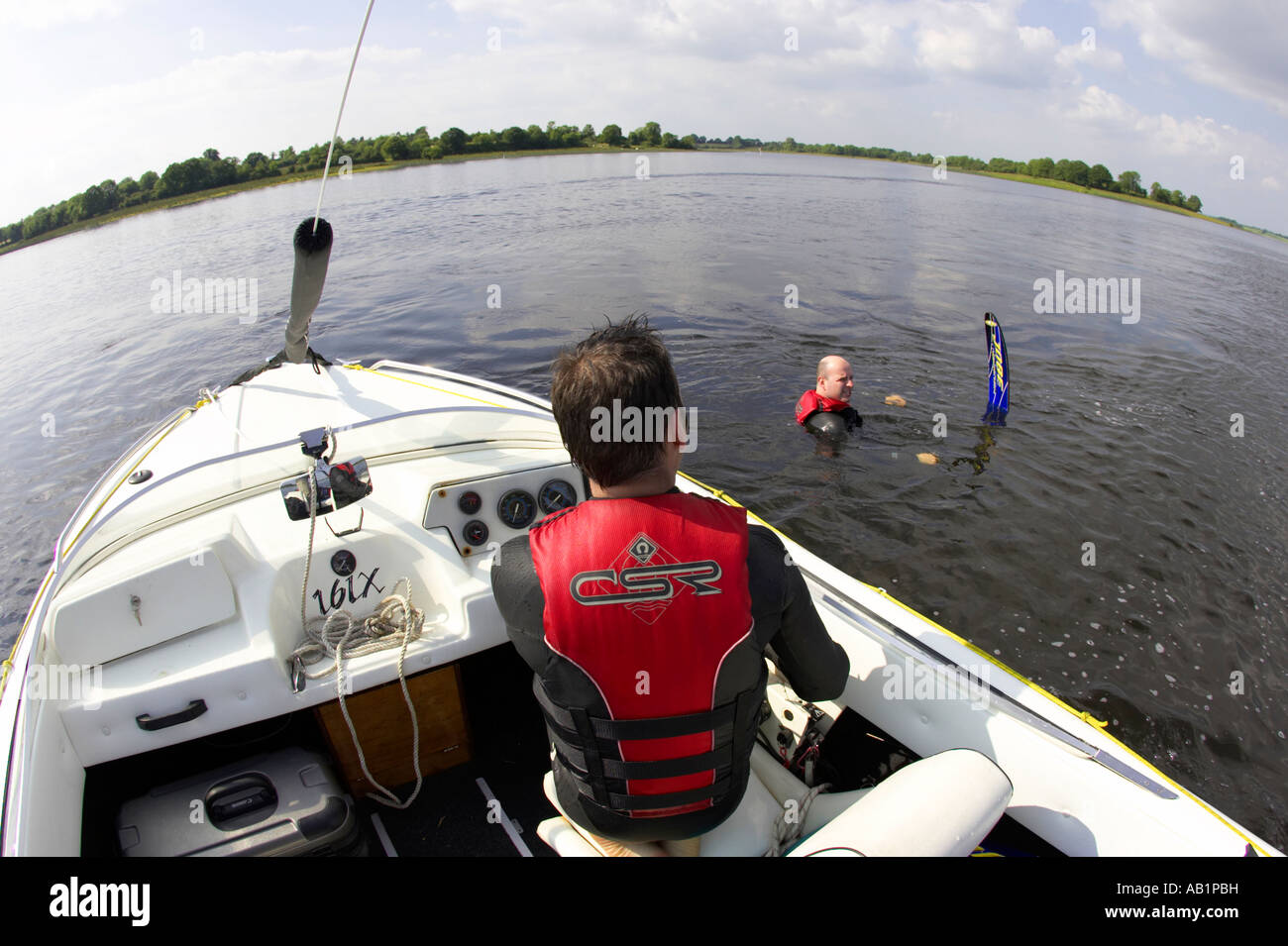 mid 30s speedboat driver drives up to waterskier floating in the water ...