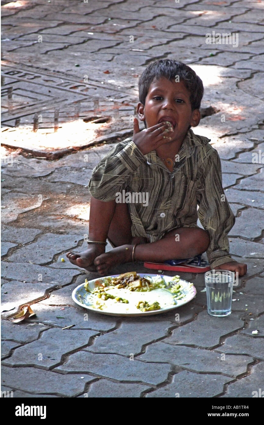 Child eating with hand sitting on pavement Mumbai Maharashtra India ...