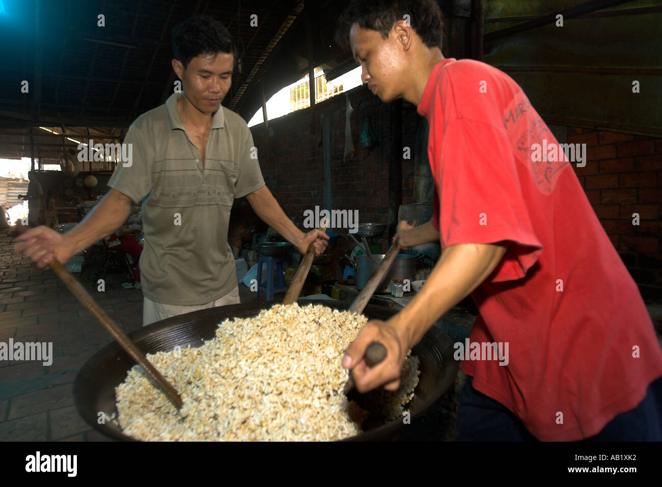 Two men with paddles mix popped rice and sugar to make rice candy crisp ...