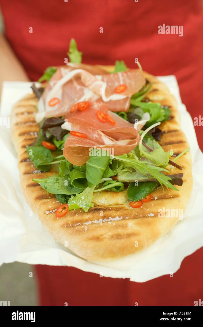 Woman holding pizza bread topped with Parma ham herbs chilli rings ...