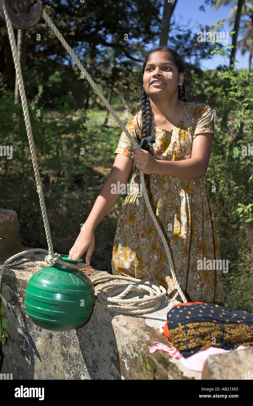 Young woman draws water from well by hand with green pot on traditional ...