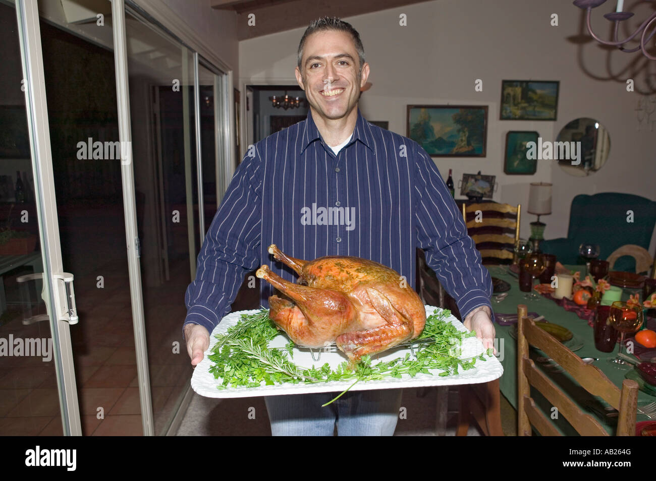 Man holds cooked turkey in front of a table set for Thanksgiving dinner ...