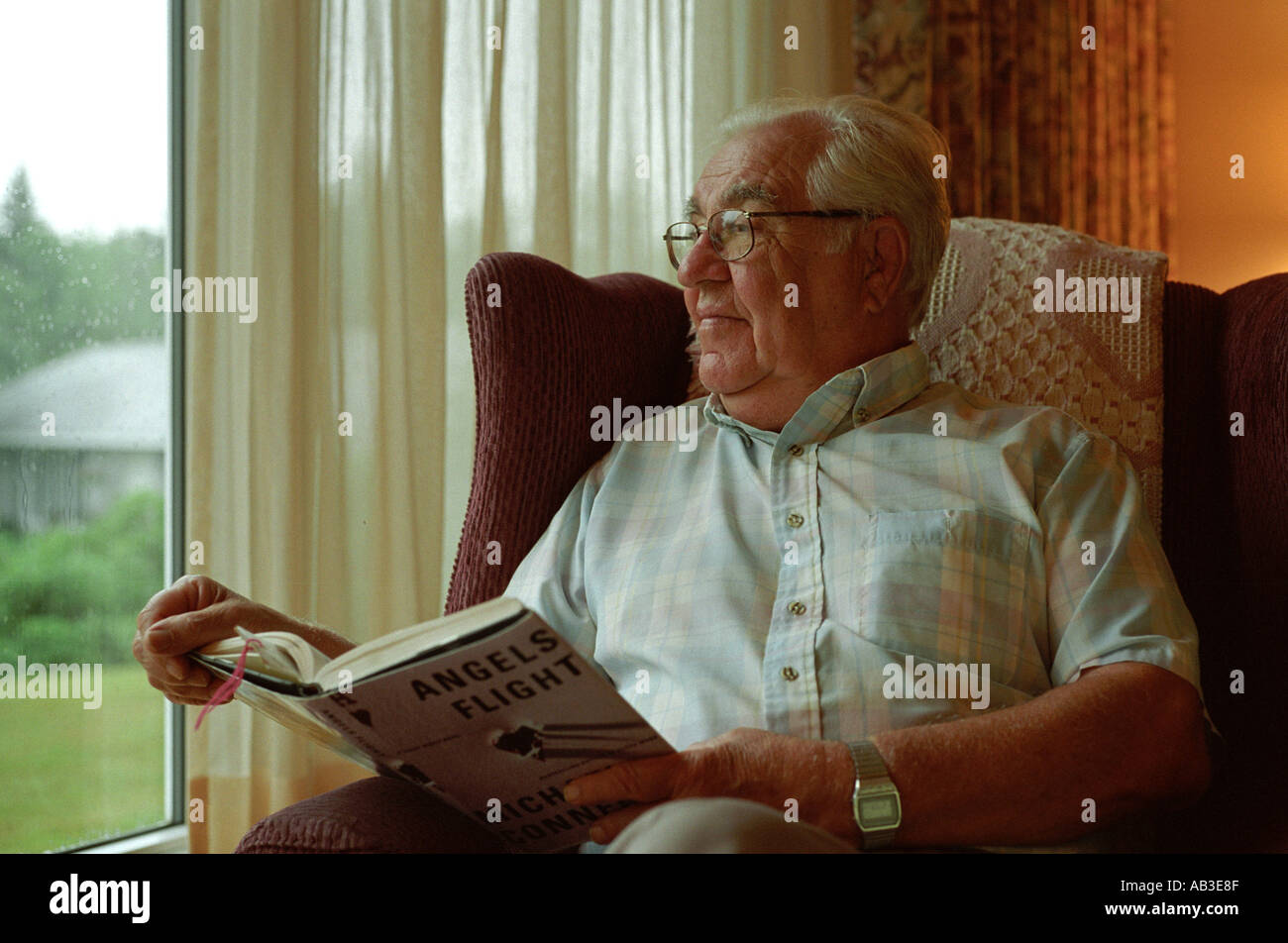 old man reading a book while waiting to go to the hospital for check up ...