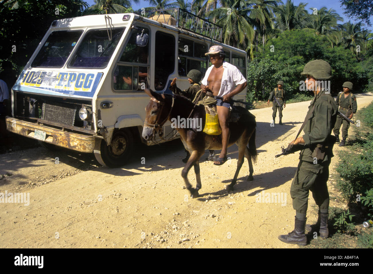 Mexican army soldiers observe a man on a donkey pass by their security ...