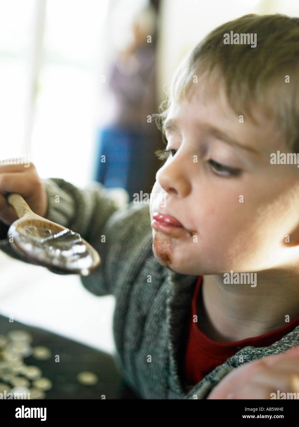 young child with wooden spoon eating chocolate icing from the mixing ...
