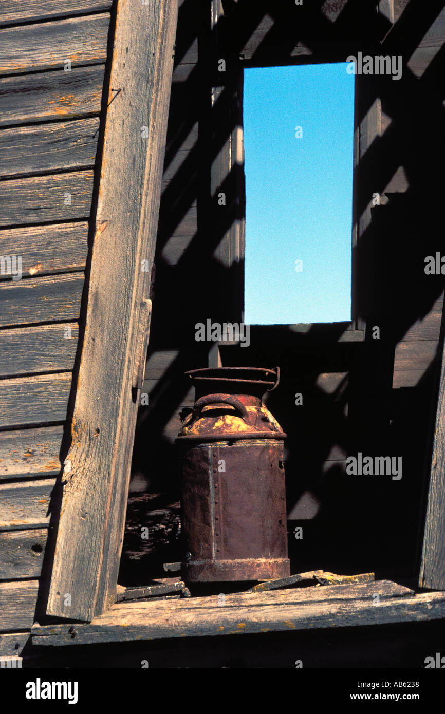 Rusty milk can with bullet holes from target practice in doorway of old ...