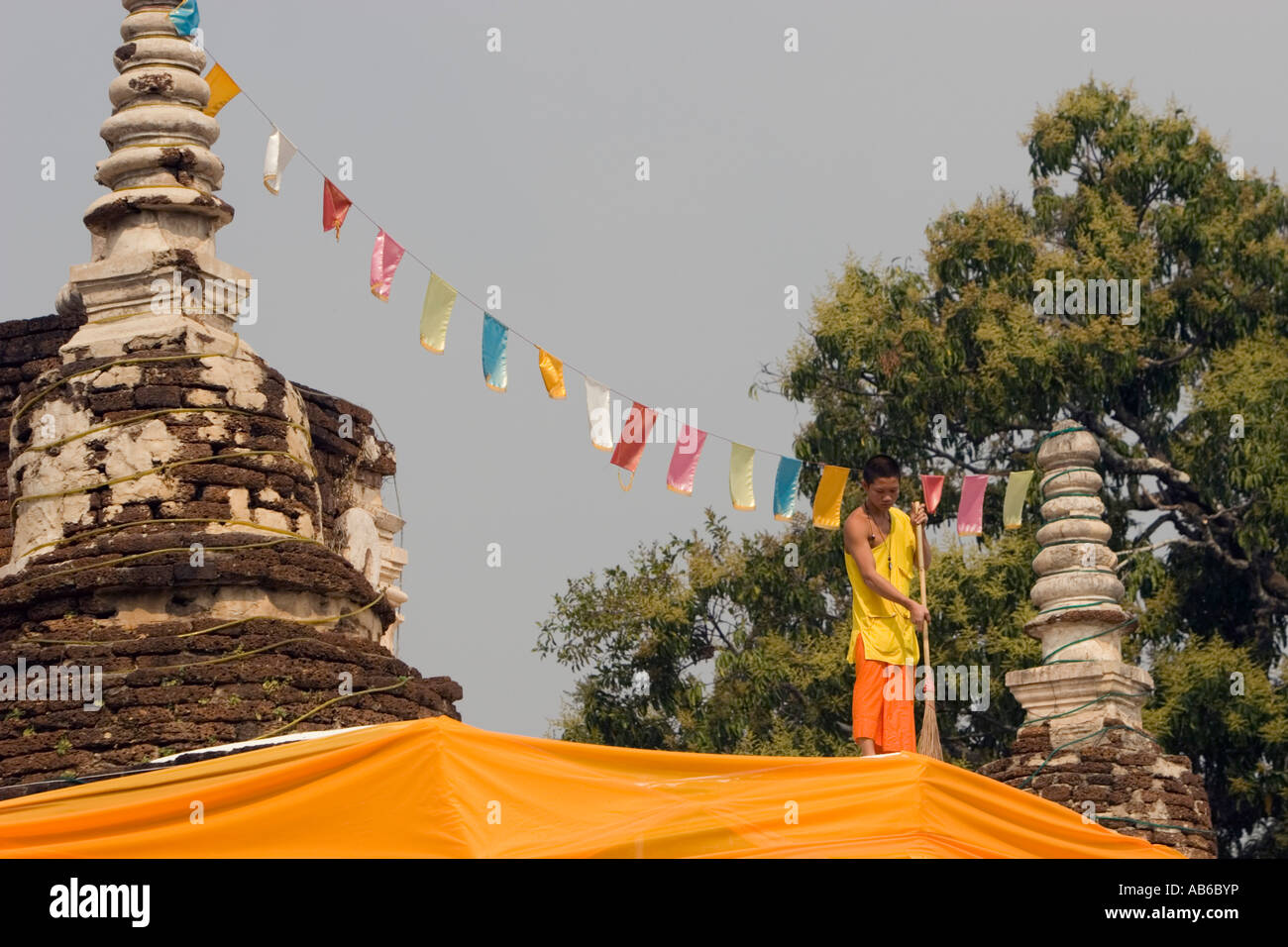 Monk sweeps up cleaning stupa with long handle broom Chiang Mai north ...