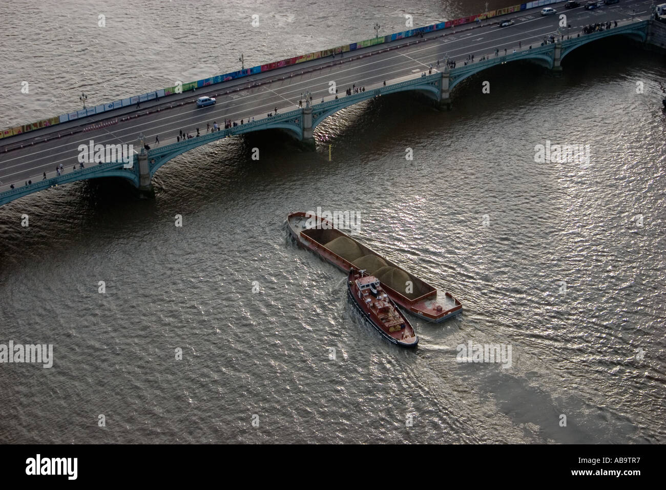 Tugboat propelling barge along the River Thames under bridge below the ...