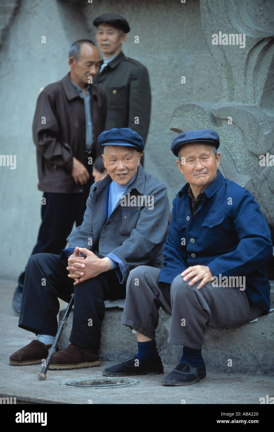 A group of senior men wearing blue Mao caps and jackets relax in a city ...