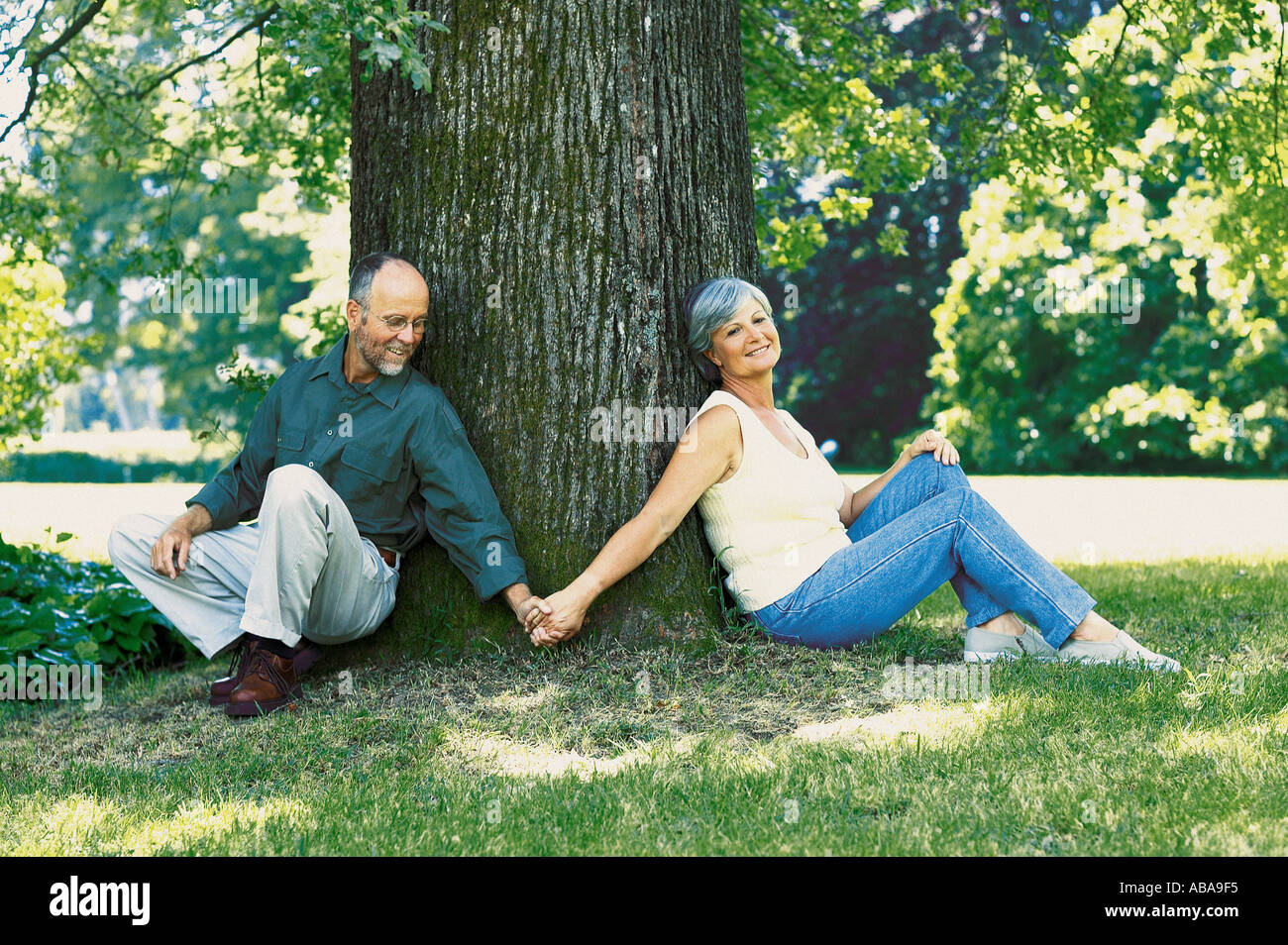 Couple sitting under tree Stock Photo - Alamy