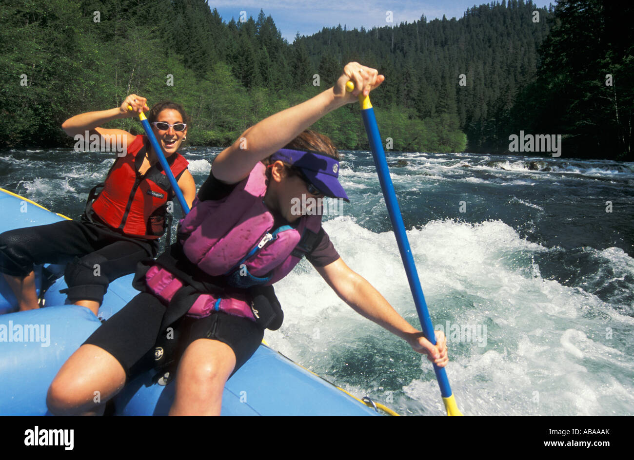 Two young women paddling inflatable raft through whitewater on the ...