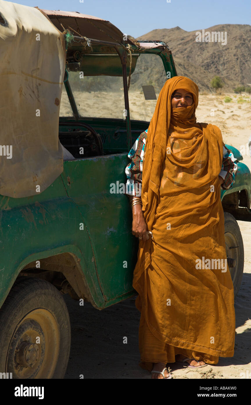 Ababda tribeswoman standing by 4x4 land rover in desert of Wadi El ...