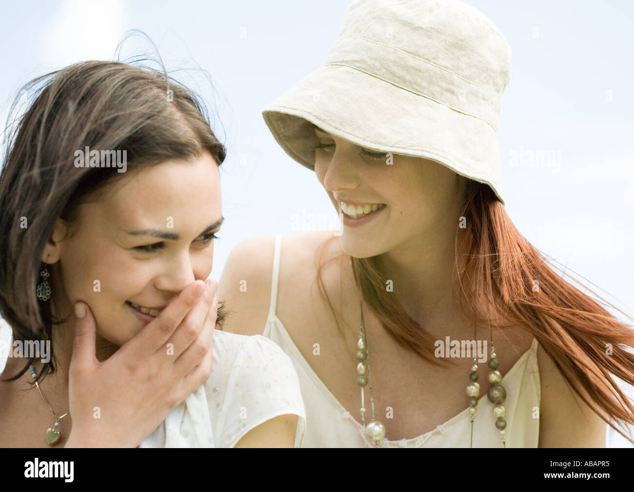 Two young women smiling, one covering mouth Stock Photo - Alamy