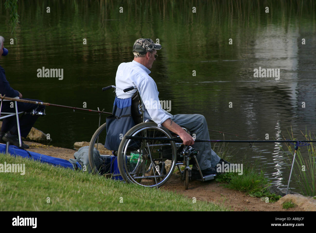 Disabled man in wheelchair on pond bank with fishing equipment enjoying ...