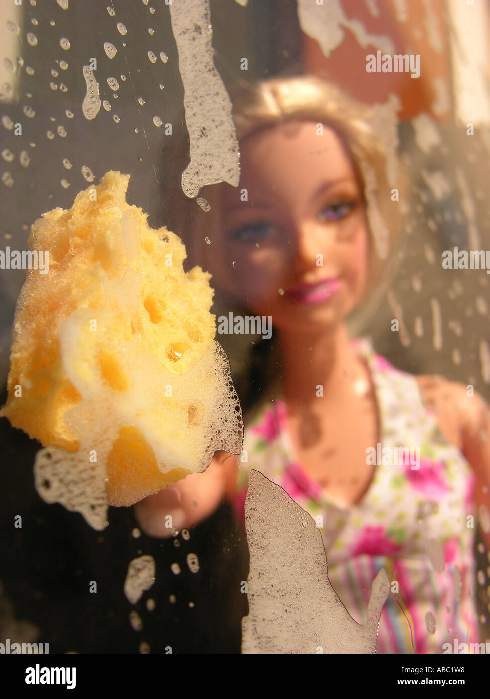 A blond Barbiepuppe cleans a window with a sponge and much soapy water ...