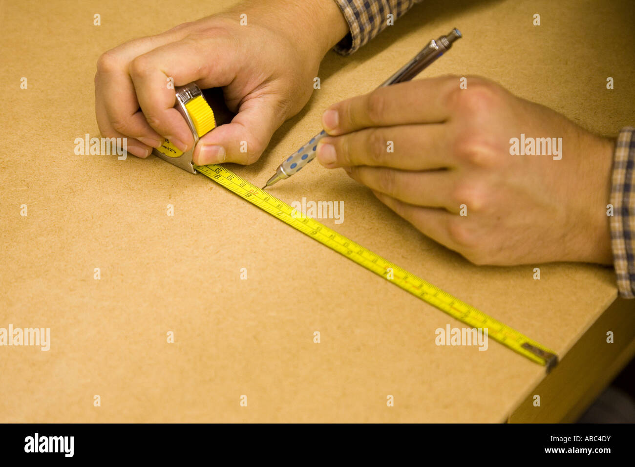 Craftsman marks out on a board of MDF with a tape measure and pencil ...