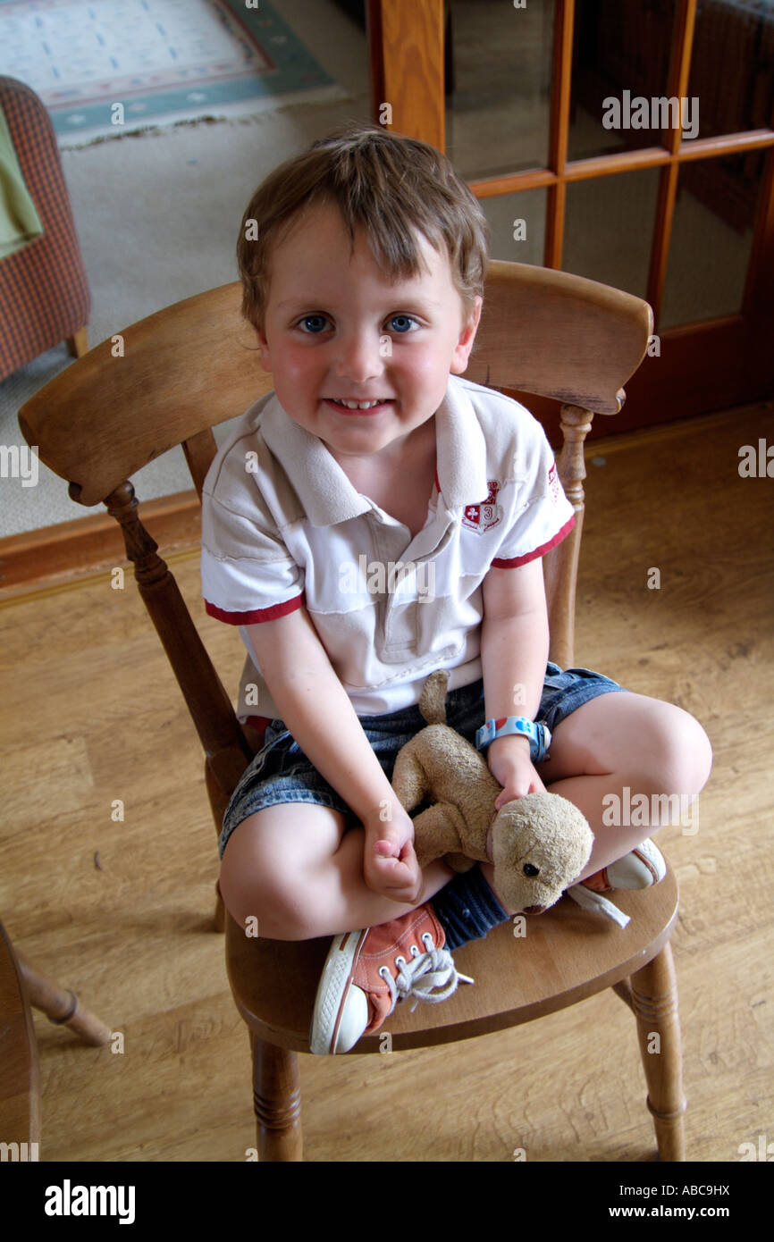 Boy sitting on a wooden chair holding a toy Stock Photo - Alamy