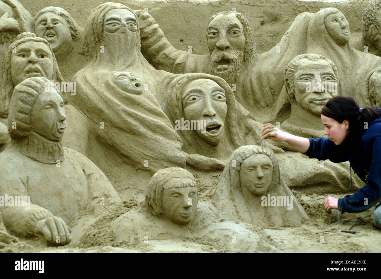 A sand sculptor creates a wall of figures in bas relief as part of a ...