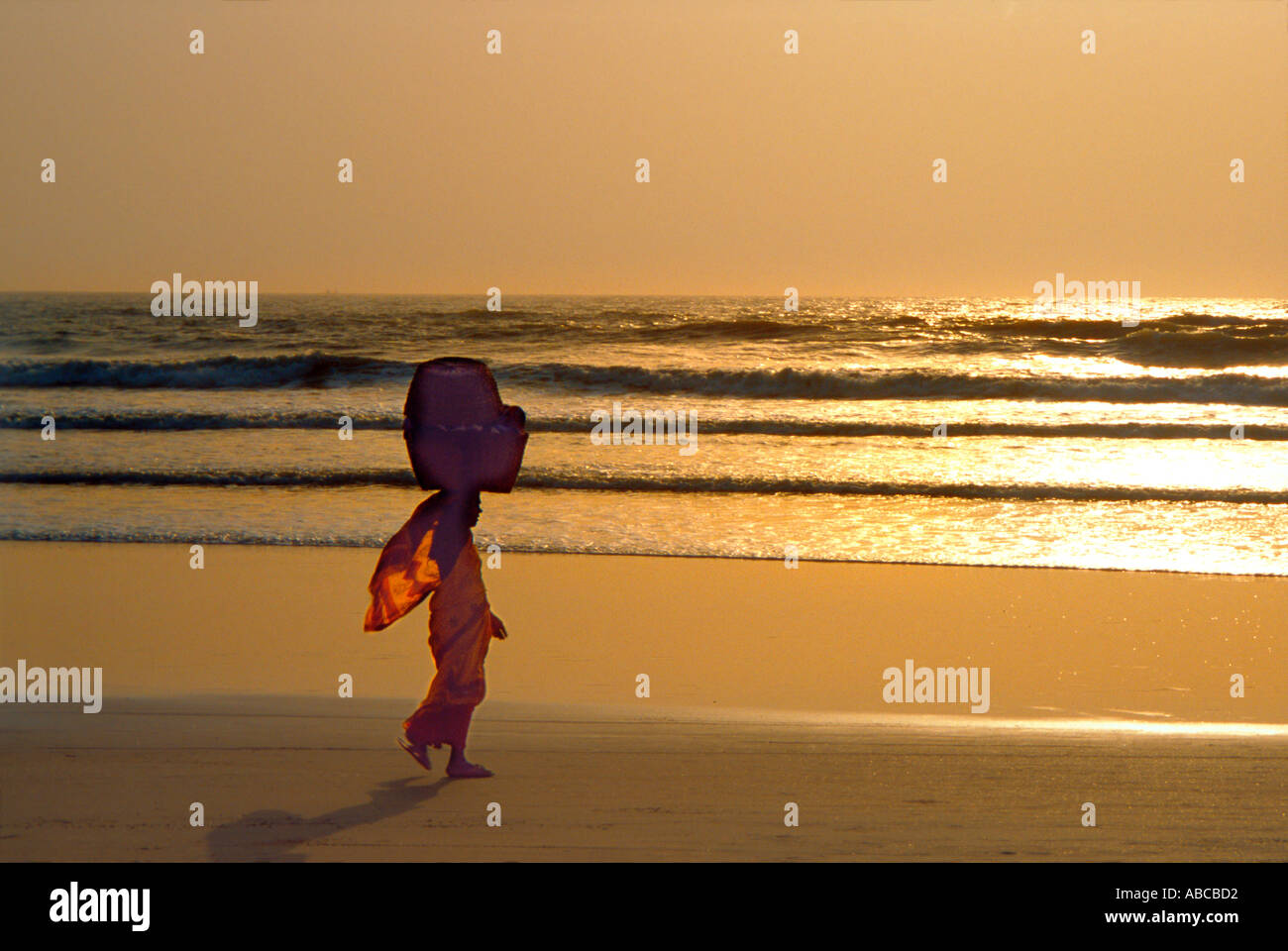 Goan woman with basket on head walks on sandy Benaulim beach. Sunset ...