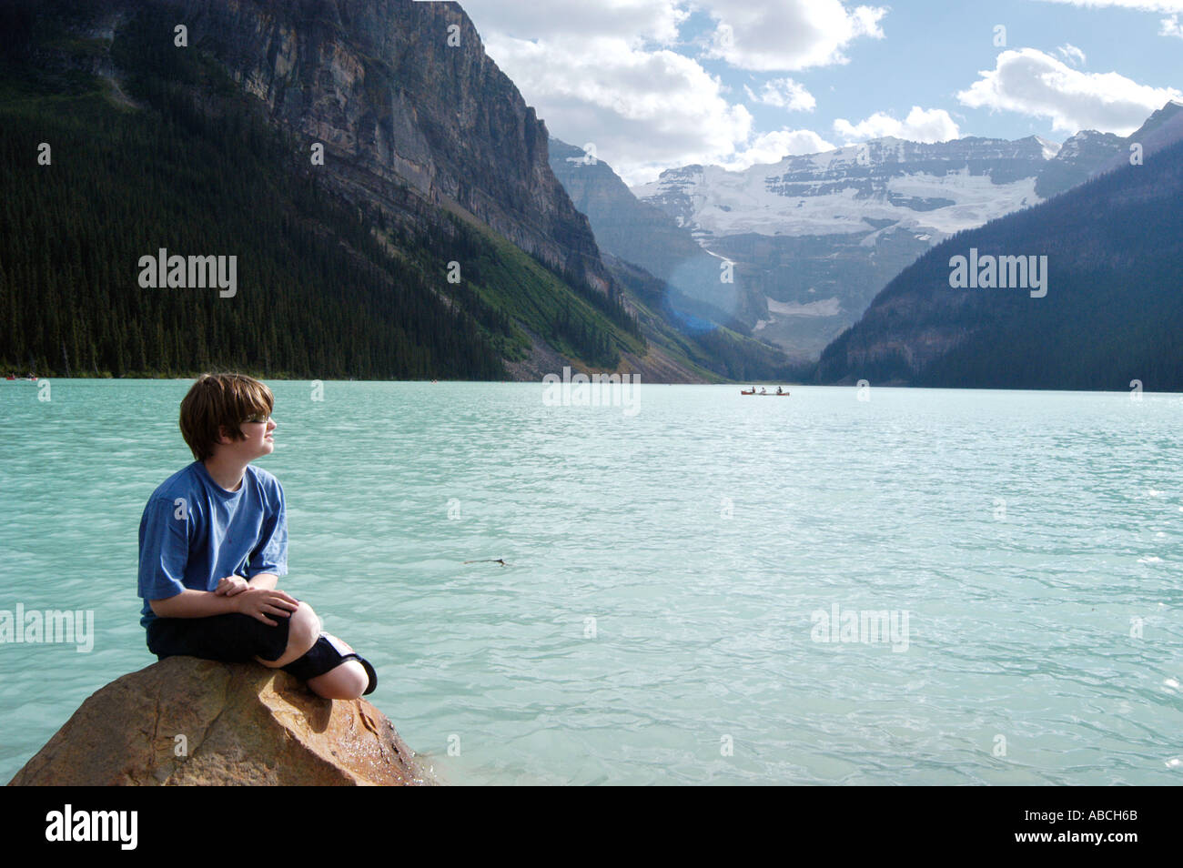 A boy sitting on a rock on the shore of Lake Louise Canadian Rockies ...