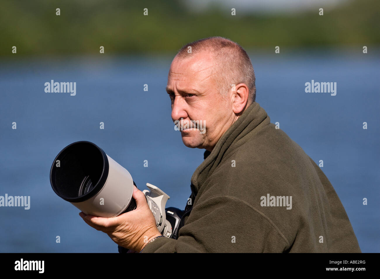 Nigel Blake standing with camera and long lens looking alert priory ...