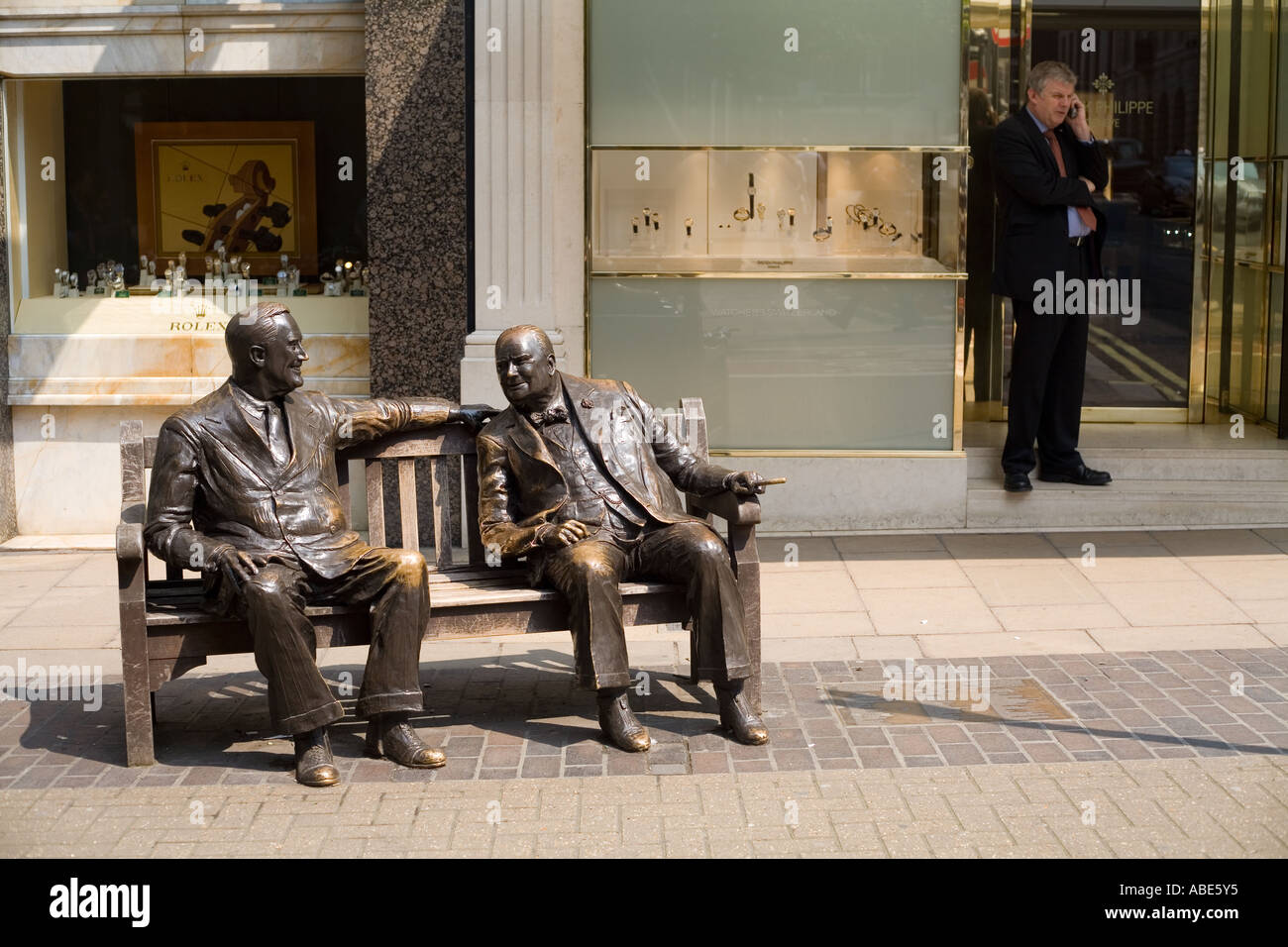 A man in a suit makes a telephone call whilst standing by a statue ...