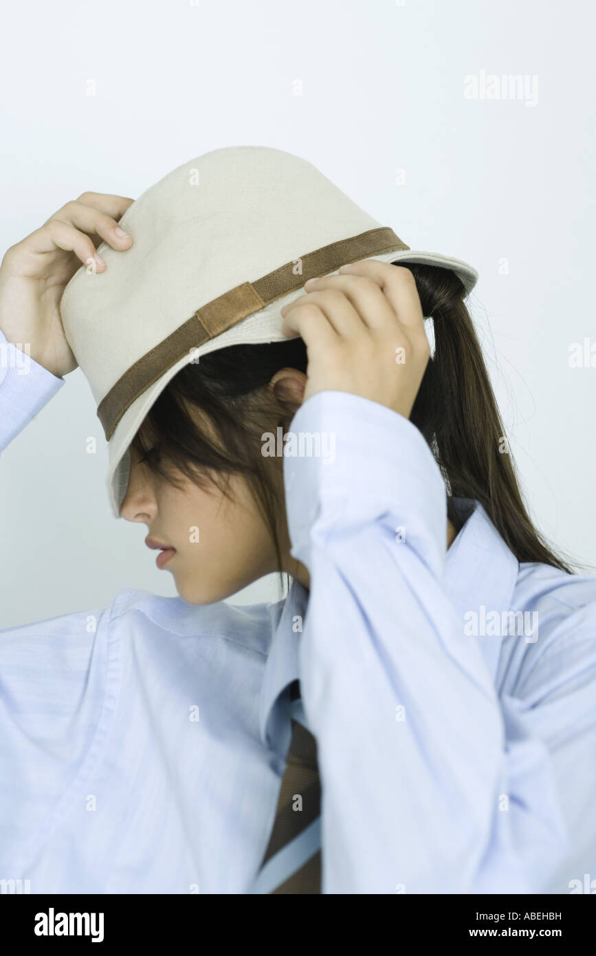Teenage girl wearing shirt and tie, pulling hat down over eyes ...