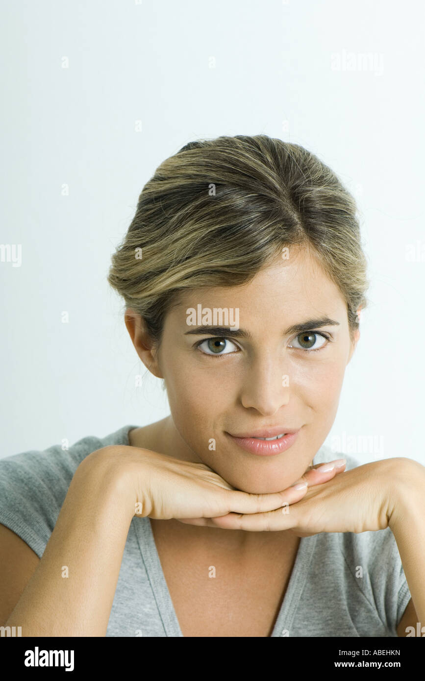 Woman, hands under chin, smiling at camera, head and shoulders ...