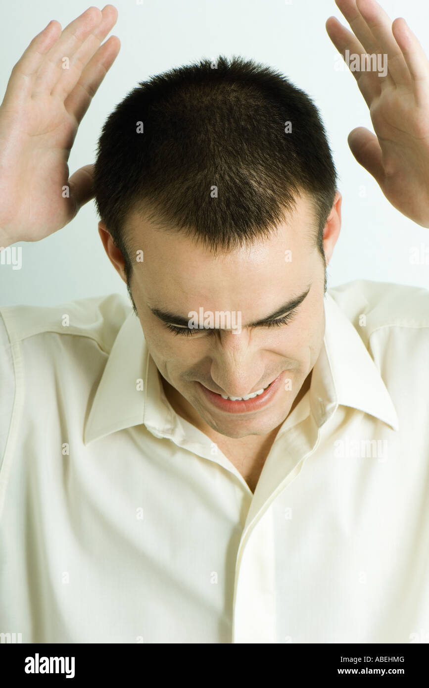 Man scowling, head down and hands up, head and shoulders, portrait ...