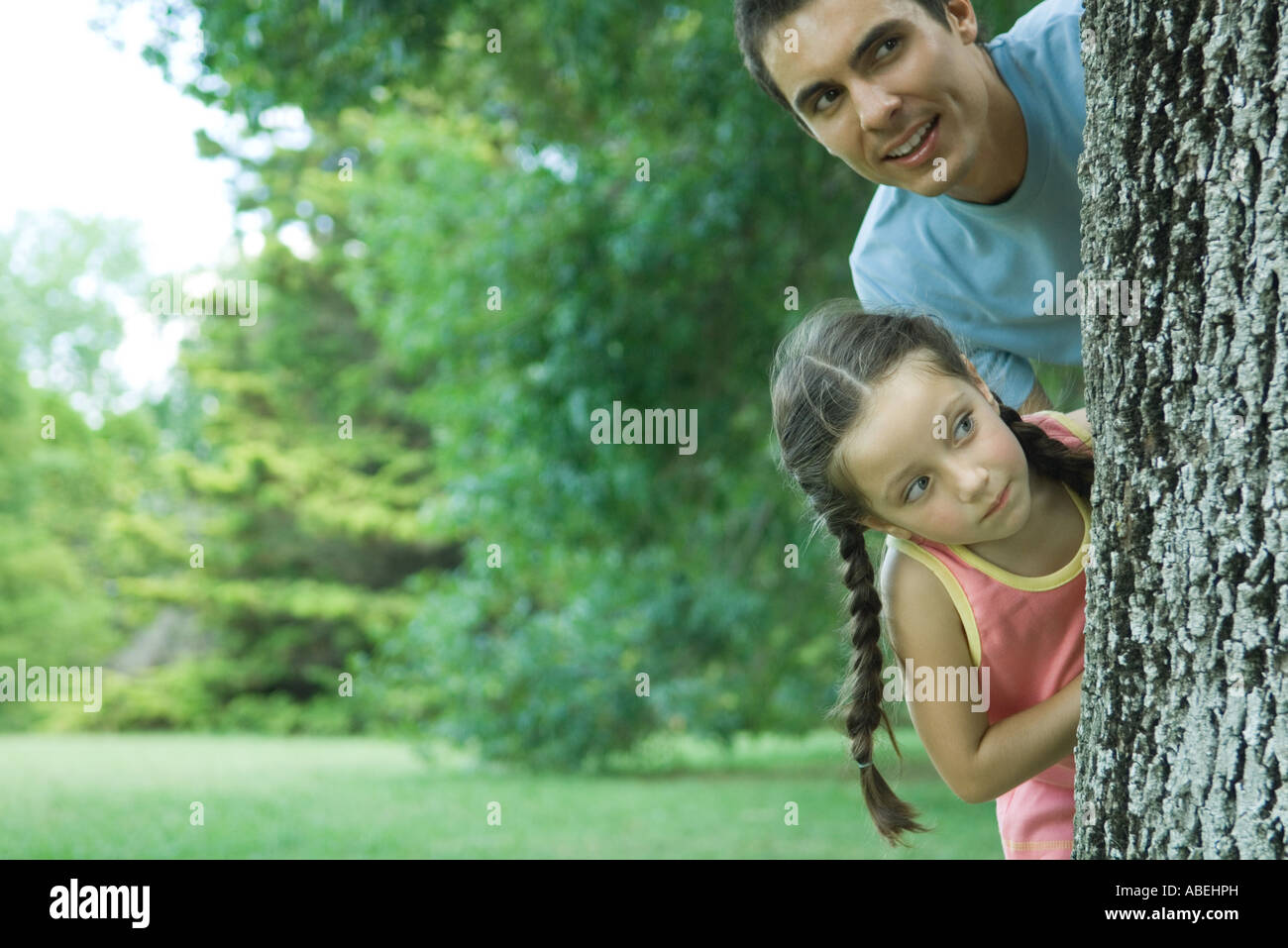 Father and daughter peeking around tree trunk Stock Photo - Alamy
