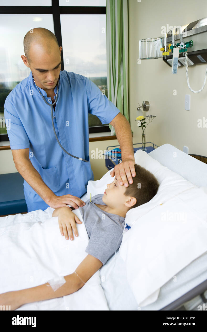 Boy lying in hospital bed, intern taking his temperature Stock Photo ...