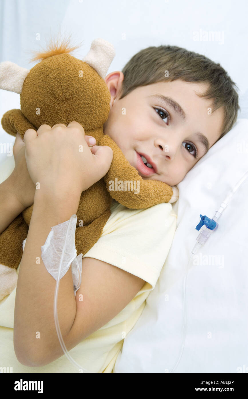 Boy lying in hospital bed with IV drip in arm, hugging stuffed animal ...